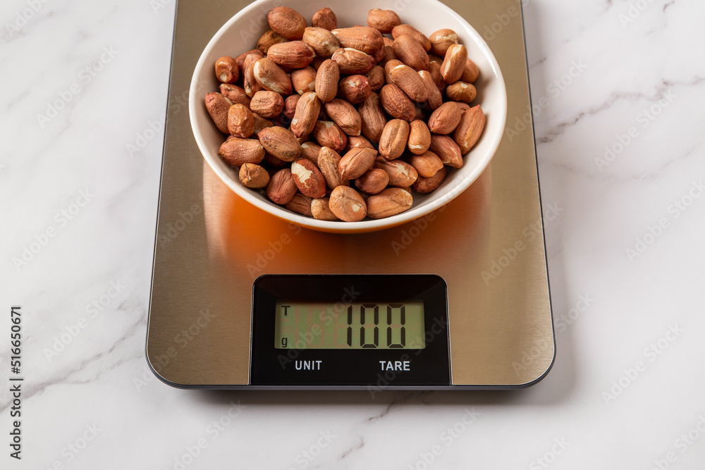 Raw dried peanut in a bowl on a digital kitchen scales. Weigh 100 g ...
