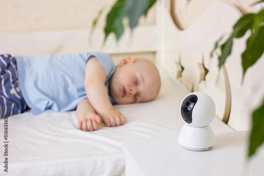 Cute little baby boy sleeping on bed at home with baby monitor camera ...