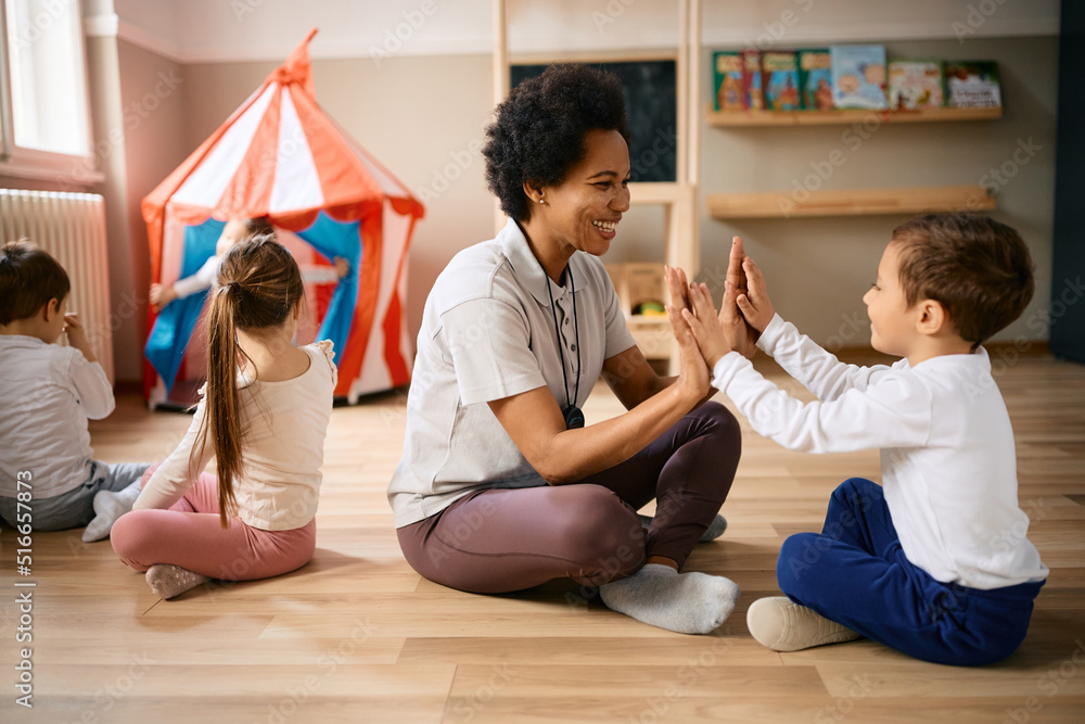 Happy black PE teacher and small boy play clapping hand game during ...