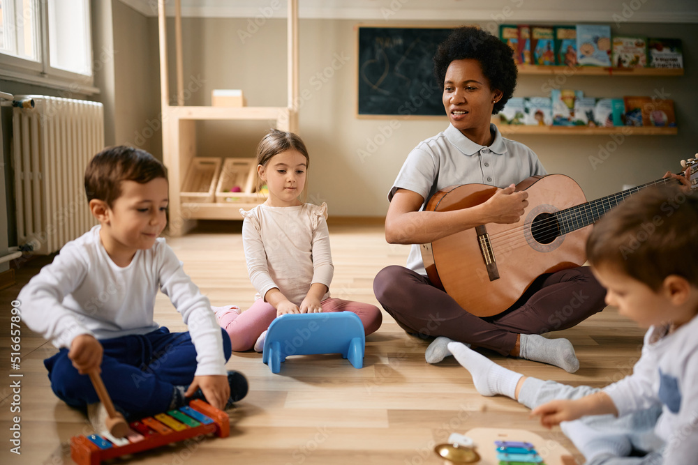 Group of children and their black female teacher playing musical ...