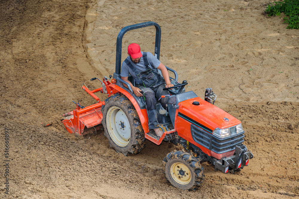 A farmer on a mini tractor loosens the soil for the lawn. Land ...