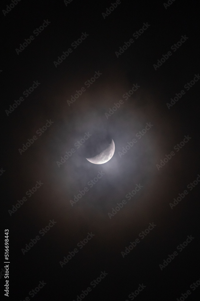 the crescent moon shining behind the cloud with a rainbow caused by the ...