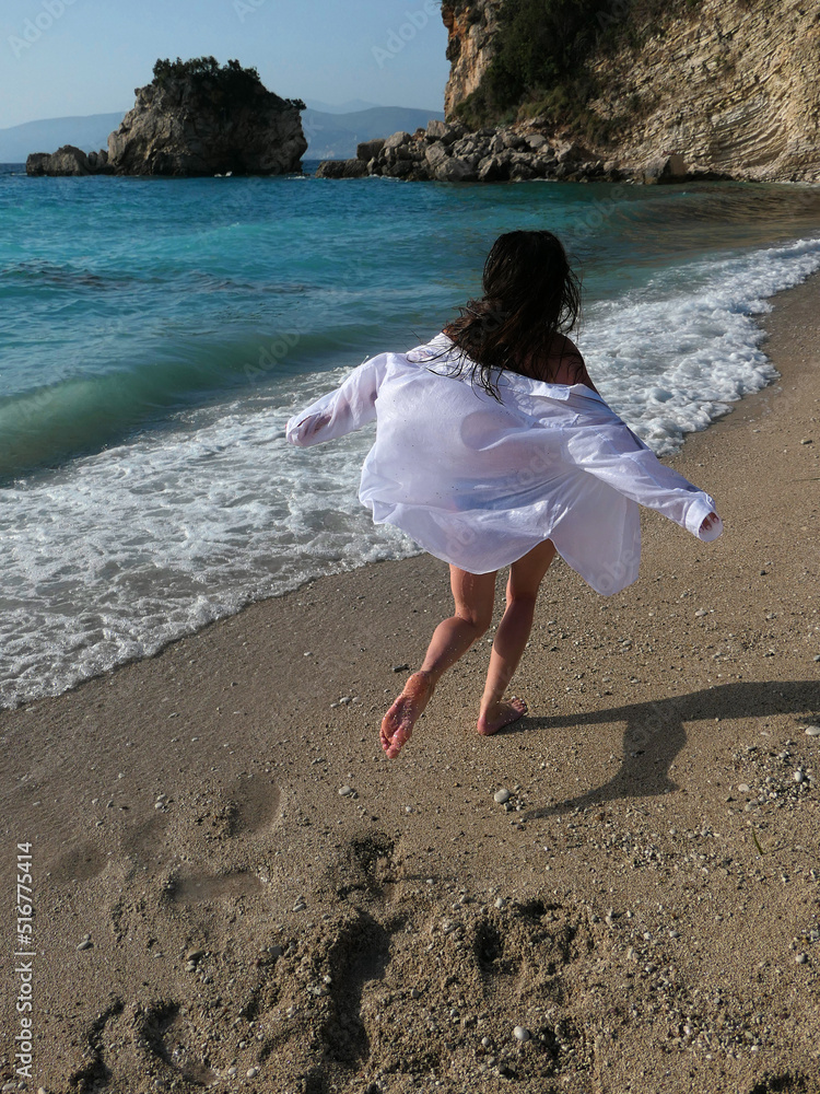 young slim beautiful woman wearing white shirt running by the sea and ...