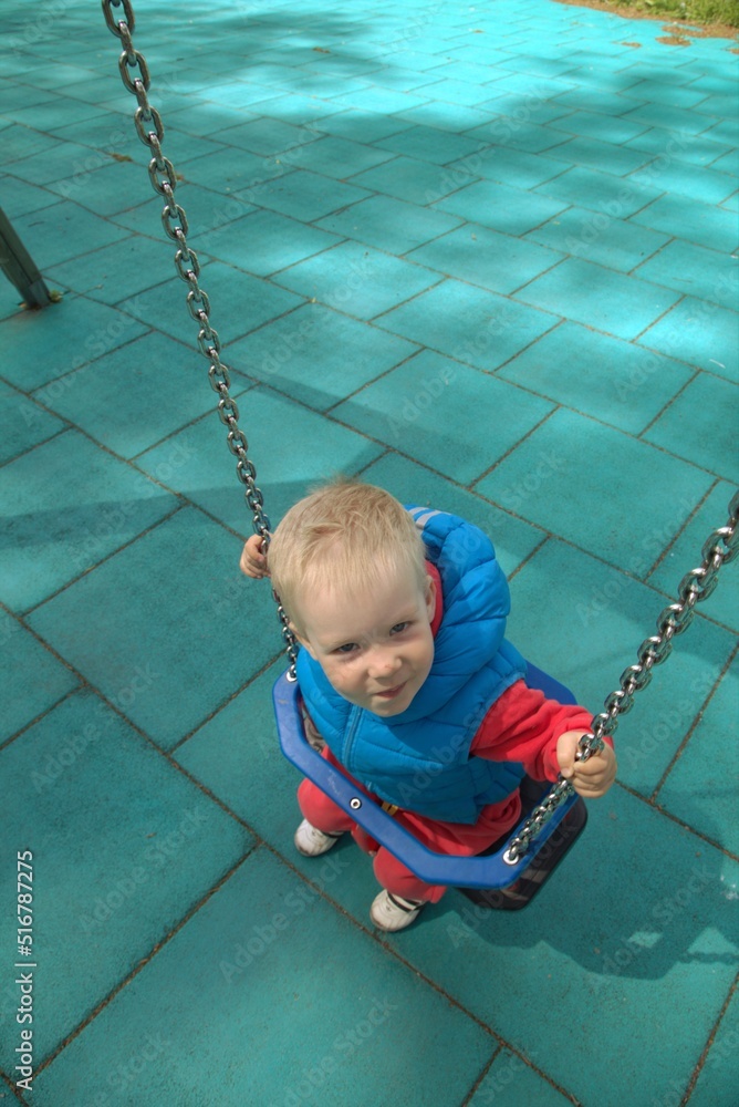 A 2 year old Blond haired Boy Plays Outside And Swings On A Swing Stock a-2-year-old-blond-haired-boy-plays-outside-and-swings-on-a-swing-stock