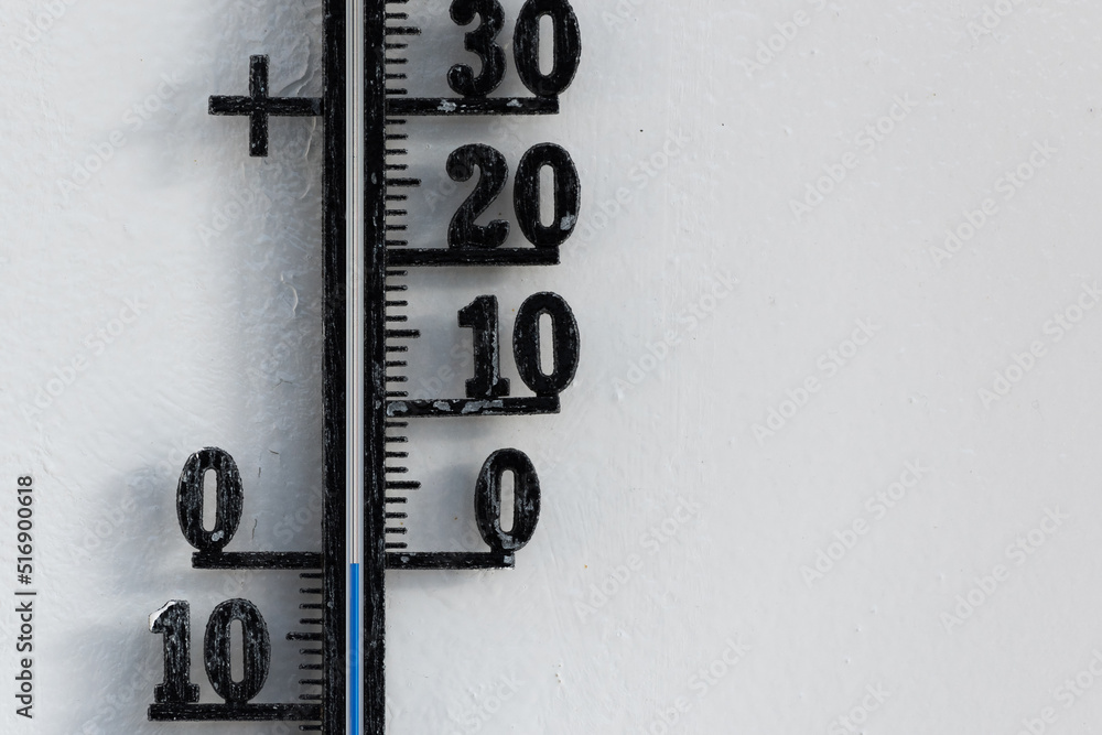 Classic black analog thermometer hanging on white wall displaying blue ...