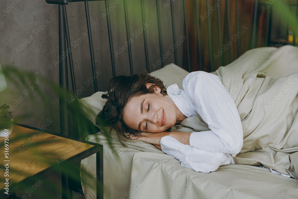 Young calm woman wear white shirt pajama she lying in bed hands folded ...