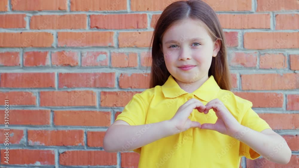 Video Stock Little girl in yellow tee shirt smiles, shows heart sign ...