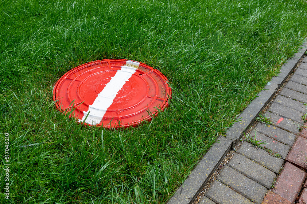 Red hatch with white stripe on green lawn. Sewer cover or fire hydrant ...