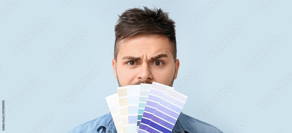 Confused young man with color palettes on light blue background Stock ...