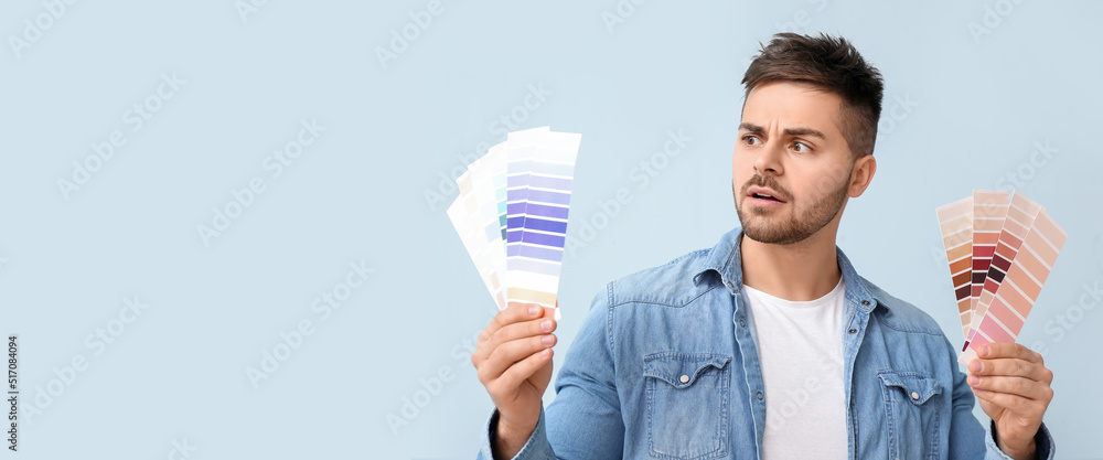 Confused young man with color palettes on light blue background with ...