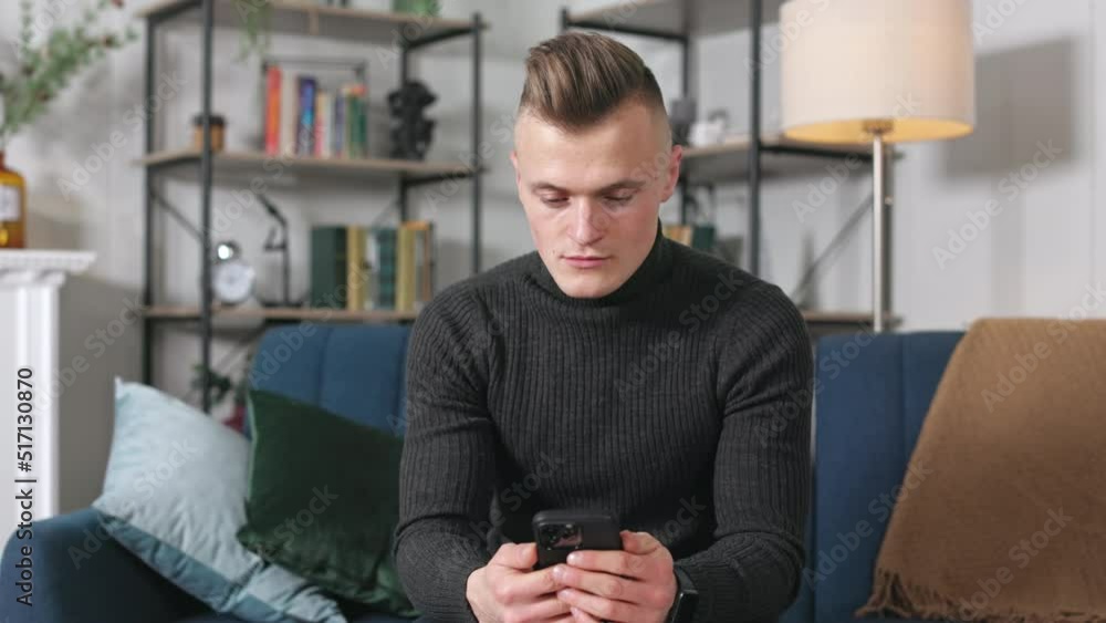 Handsome young man sitting on sofa and texting messages on modern ...