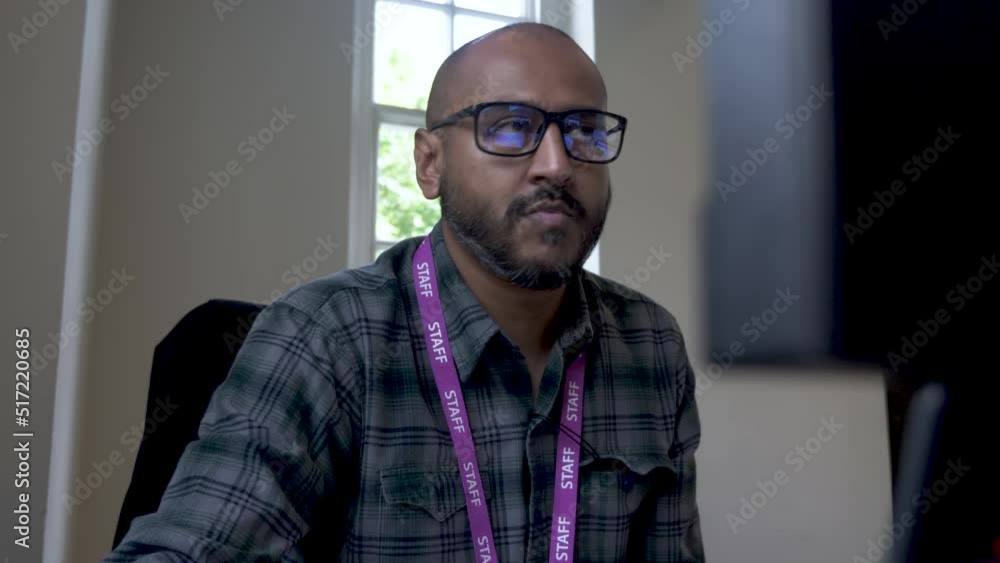 A close up shot from behind an office desk of an Indian man wearing ...