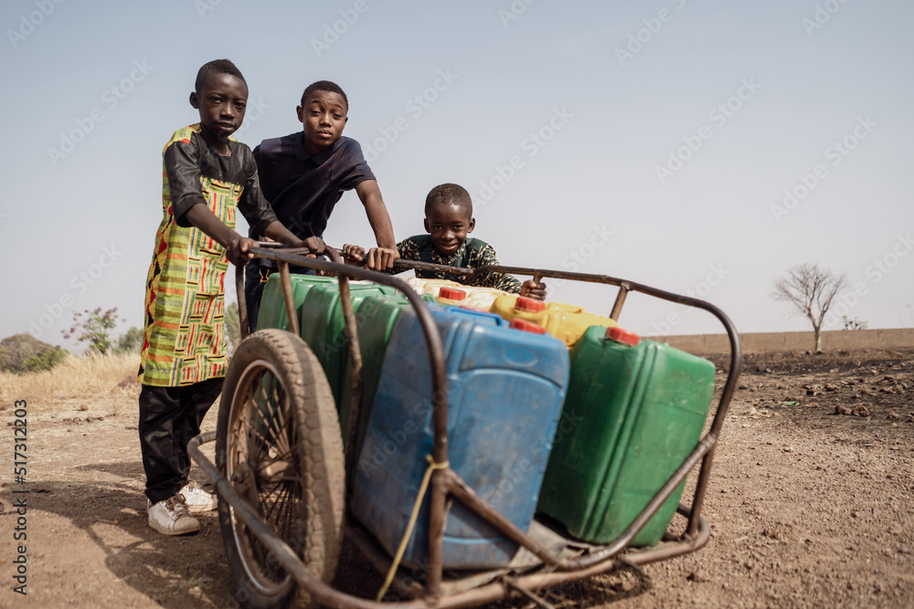 Group of young African boys pushing a heavy cart full of water cans ...