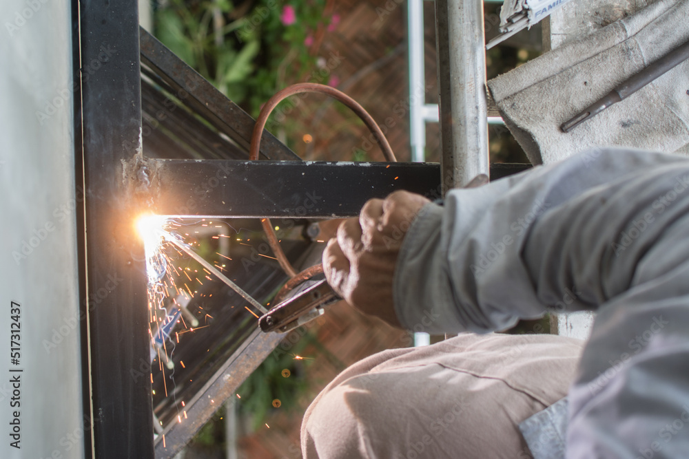 worker welds the steel structure of the roof at the construction site ...