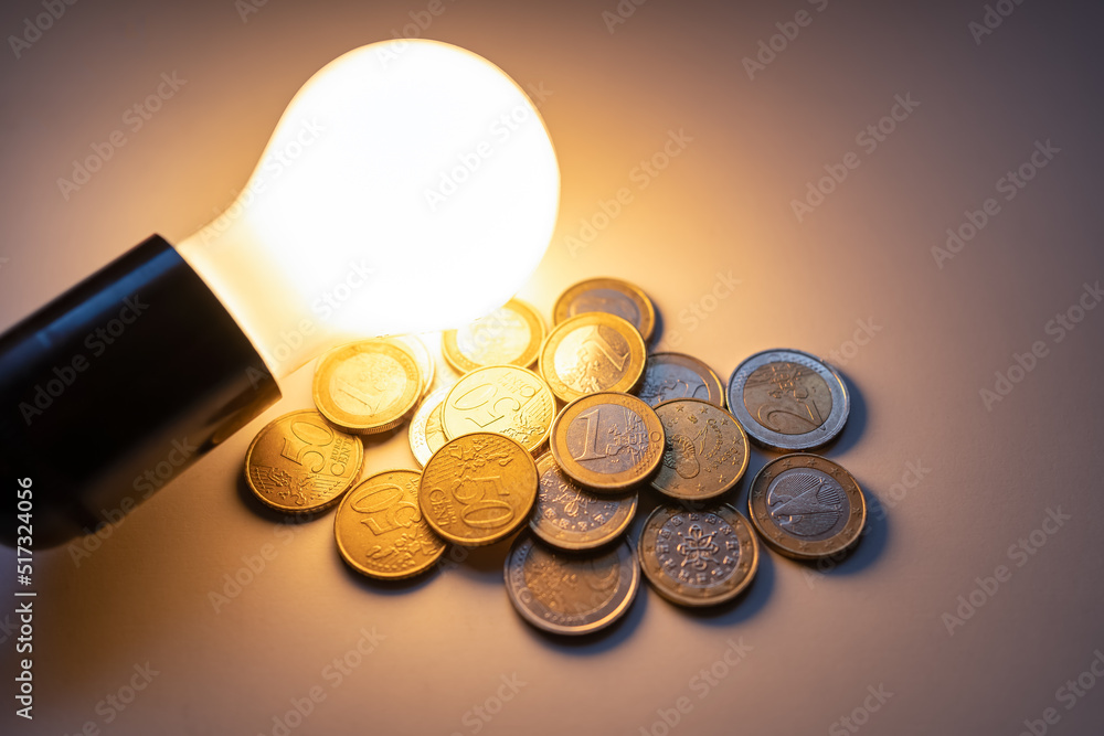 Fotka „Light bulb lit illuminating coins for the high cost of ...