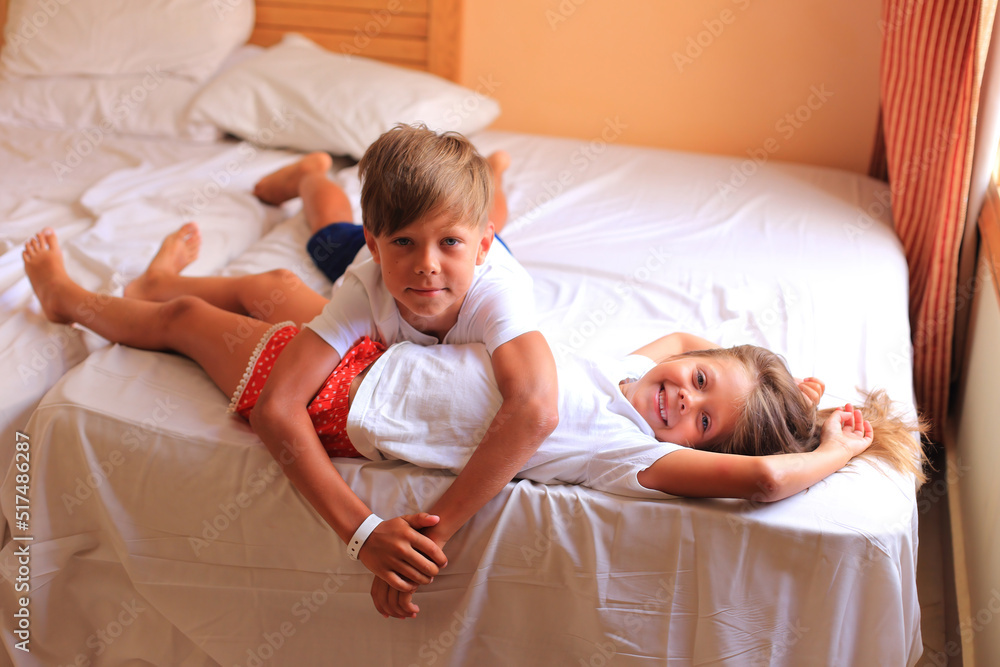 Two children lie on a bed with white sheets in a hotel room on vacation ...
