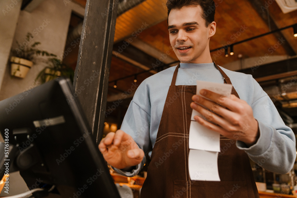 Young waiter man standing in front of computer and holding receipt ...