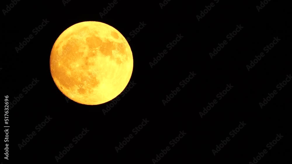 Glowing yellow huge full moon as seen from earth through the clouds ...