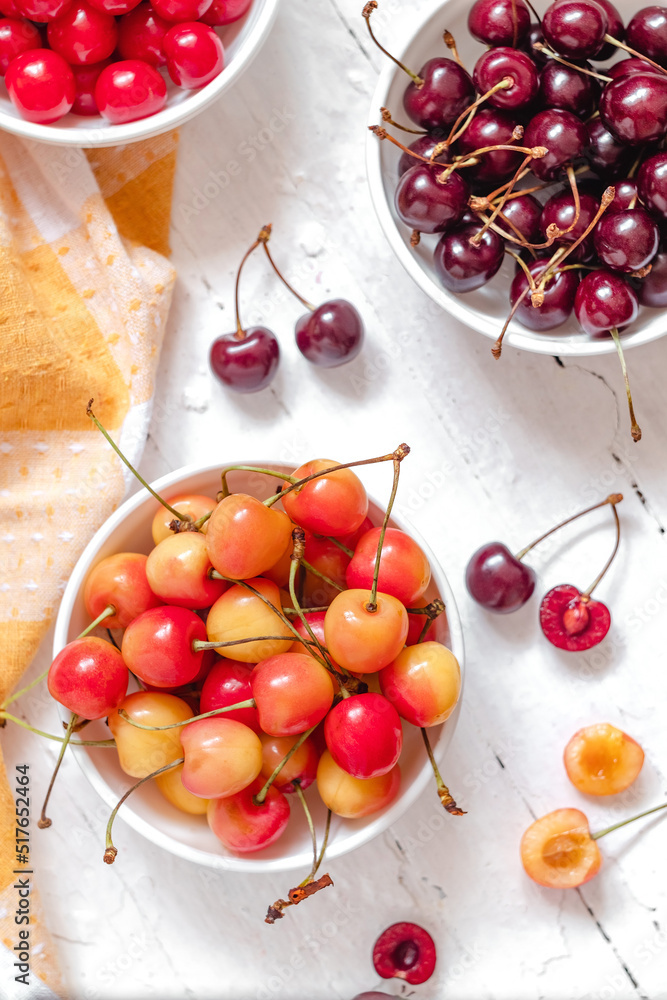 Yellow and red cherries in white bowls on a white background. Top view ...