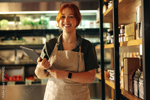 Happy young grocery store owner smiling at the camera in her shop ...