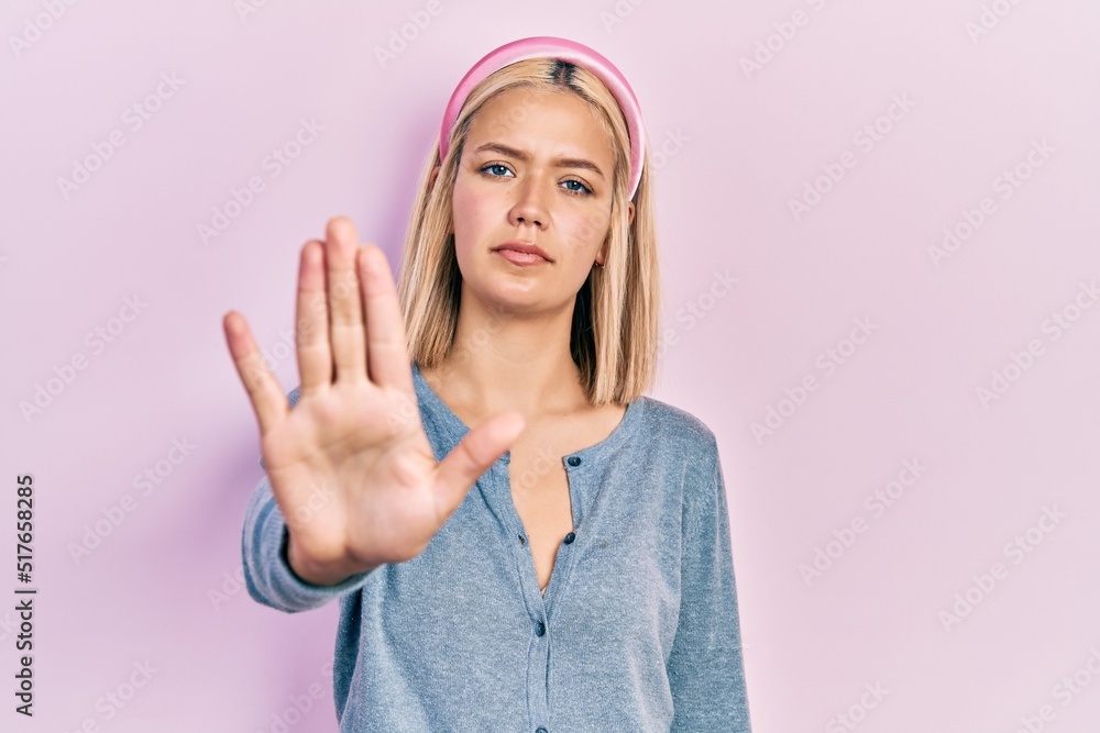 Beautiful blonde woman standing over pink background doing stop sing ...