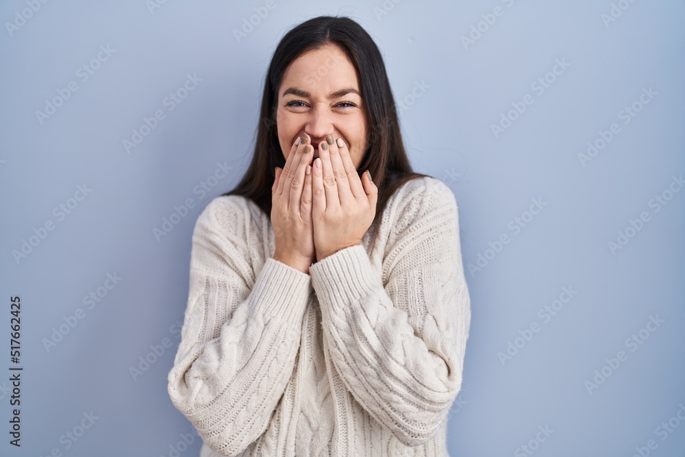 Young brunette woman standing over blue background laughing and ...