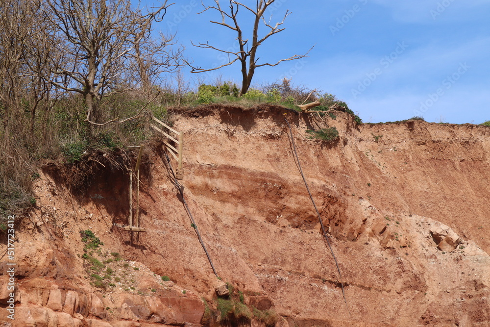 Garden fences hang dangerously over the edge of the red sandstone ...