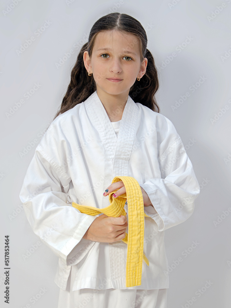 Ten Year Old Girl In A White Kimono Tying A Yellow Belt Looking At The