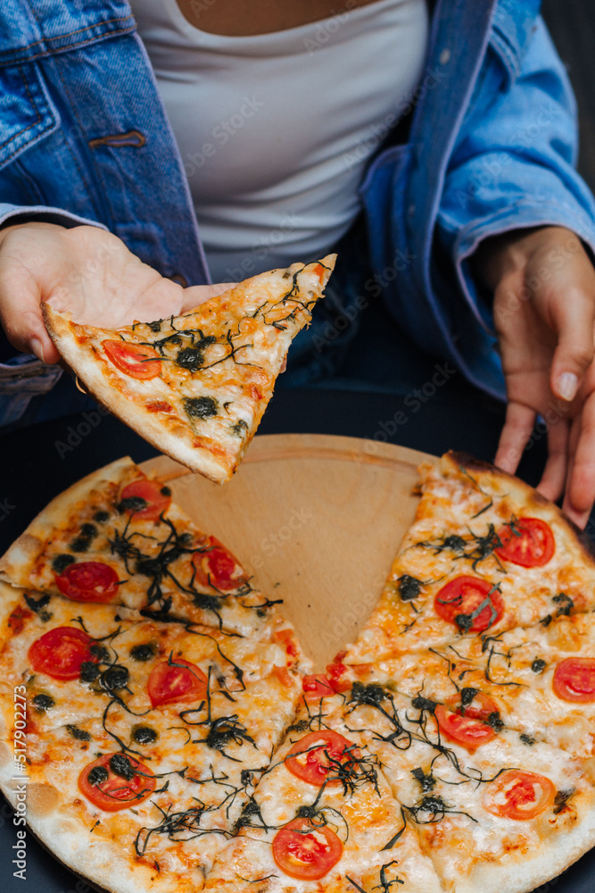 Hand taking a slice of pizza from table. Big pizza without one piece ...