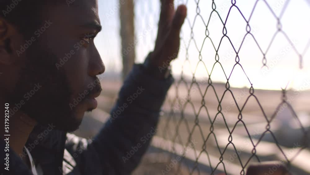 Male prisoner looking through a wire fence thinking about life and ...