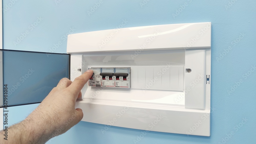 Circuit breaker board displays many switches. A finger is about to turn ...