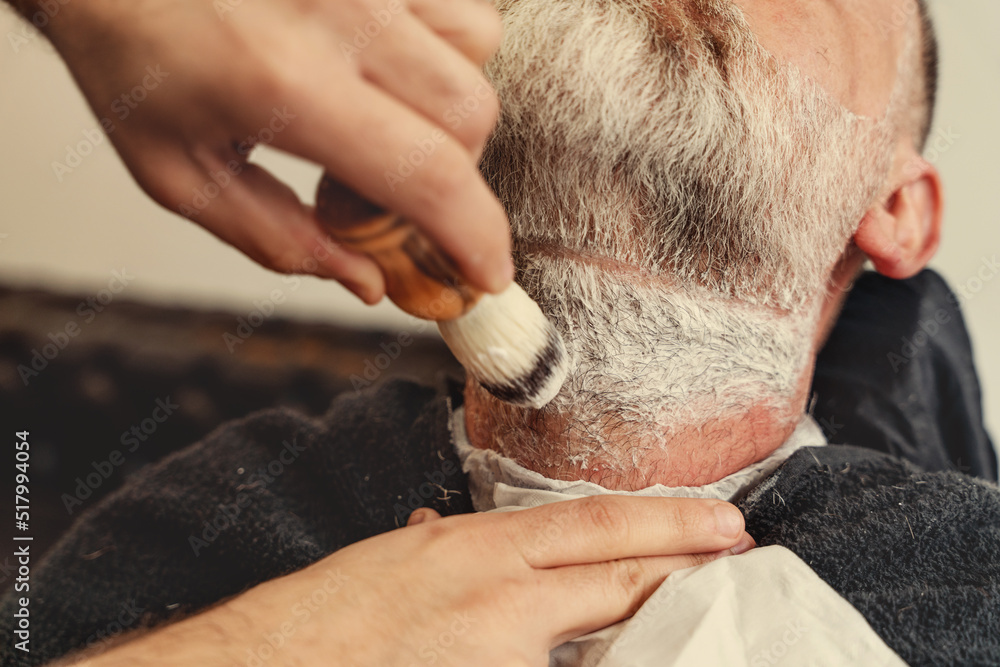 Shaving with a straight razor in a barbershop. A bearded old man being ...