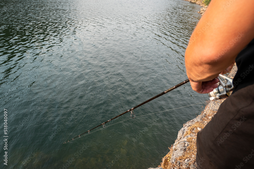 Pescador com a sua cana de pesca sobre a água junto à margem do rio ...
