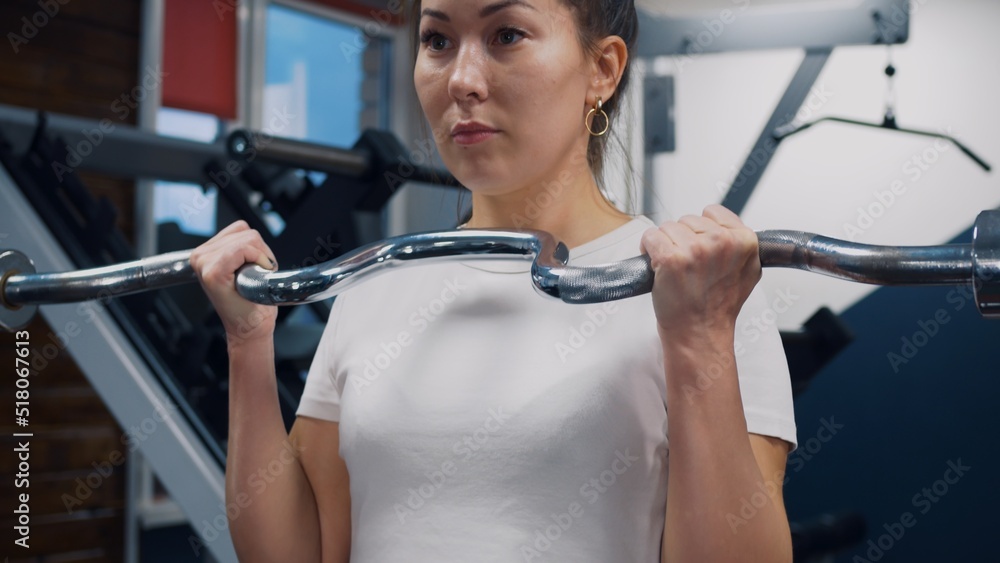 A slender woman in the gym lifts a barbell to pump up muscles. Dynamic ...