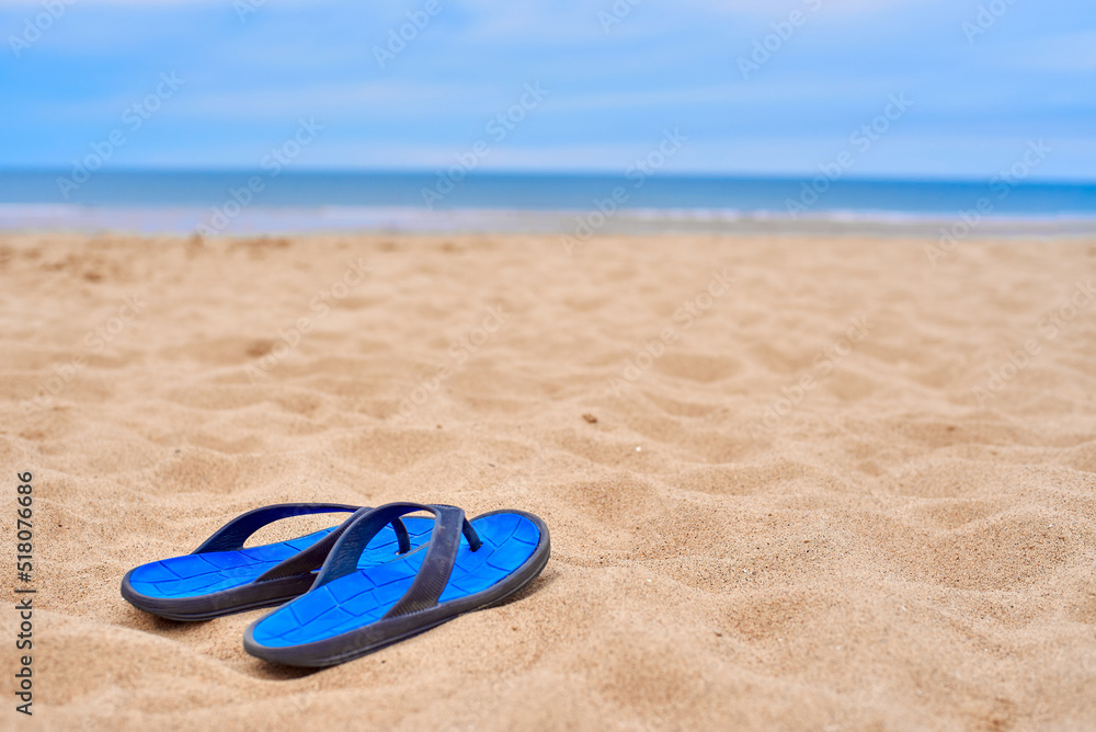 Men's rubber flip-flops stand on beautiful yellow sand. The concept of ...