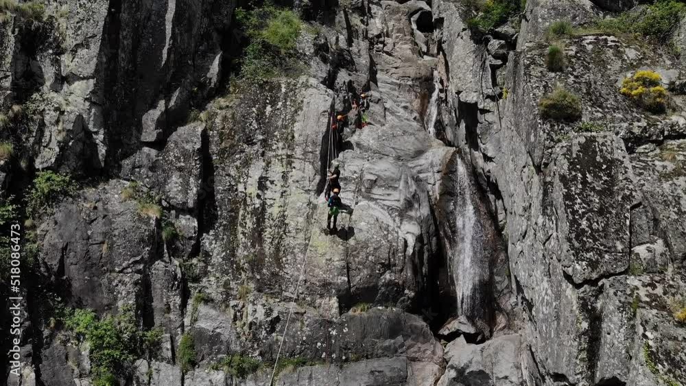 Unrecognizable people abseiling while canyoning. two rock climbers hanging off of ropers above a ...