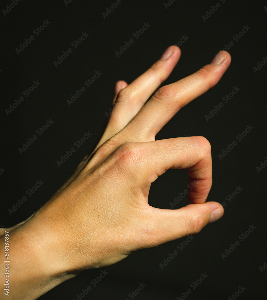 The man's hand is isolated on a dark background and shows the "OK" sign ...