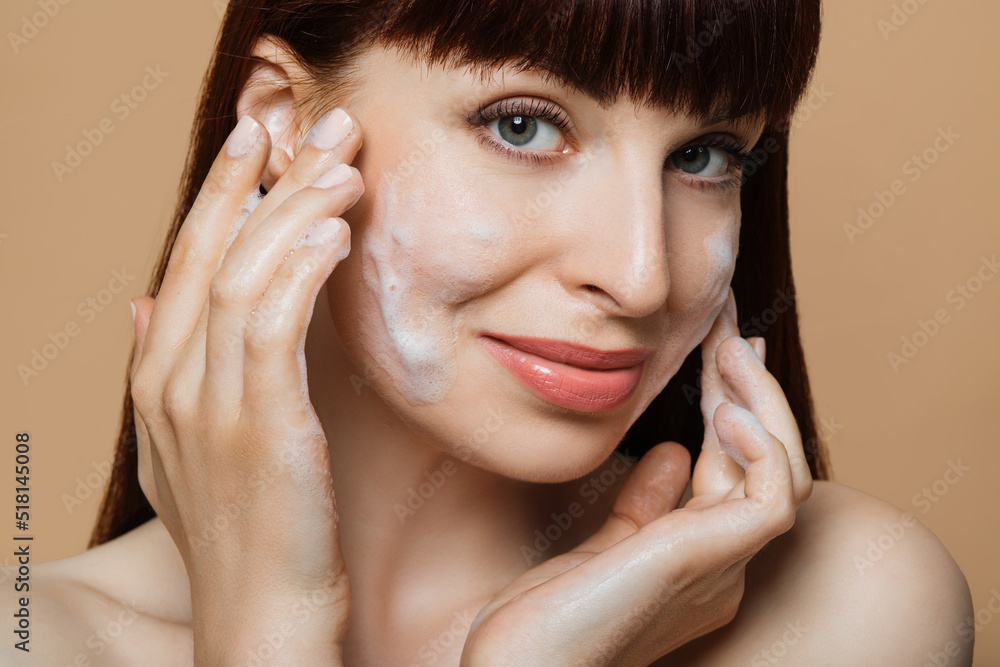 Happy smiling young woman cleaning face with soap foam studio portrait ...