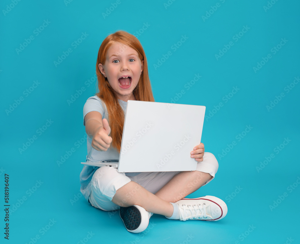 Little red headed girl sitting with legs crossed using laptop and ...