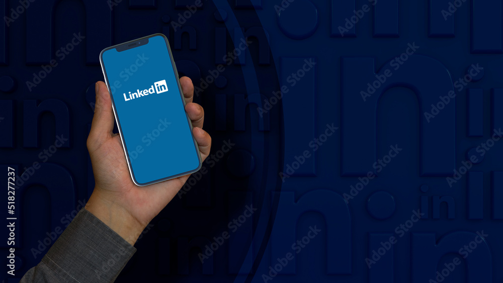 A male hand holding a smart phone displaying the Linkedin logo on its ...
