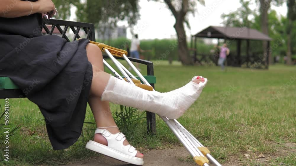 A young girl with a cast and crutches is sitting in the park, watching ...