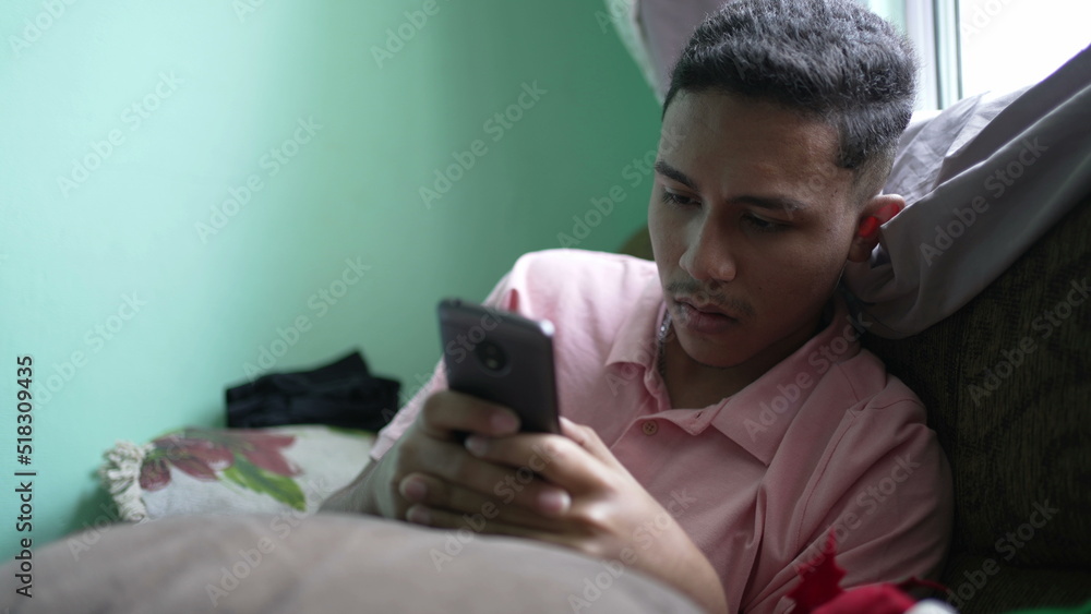 One hispanic man looking at phone screen sitting on couch at home ...