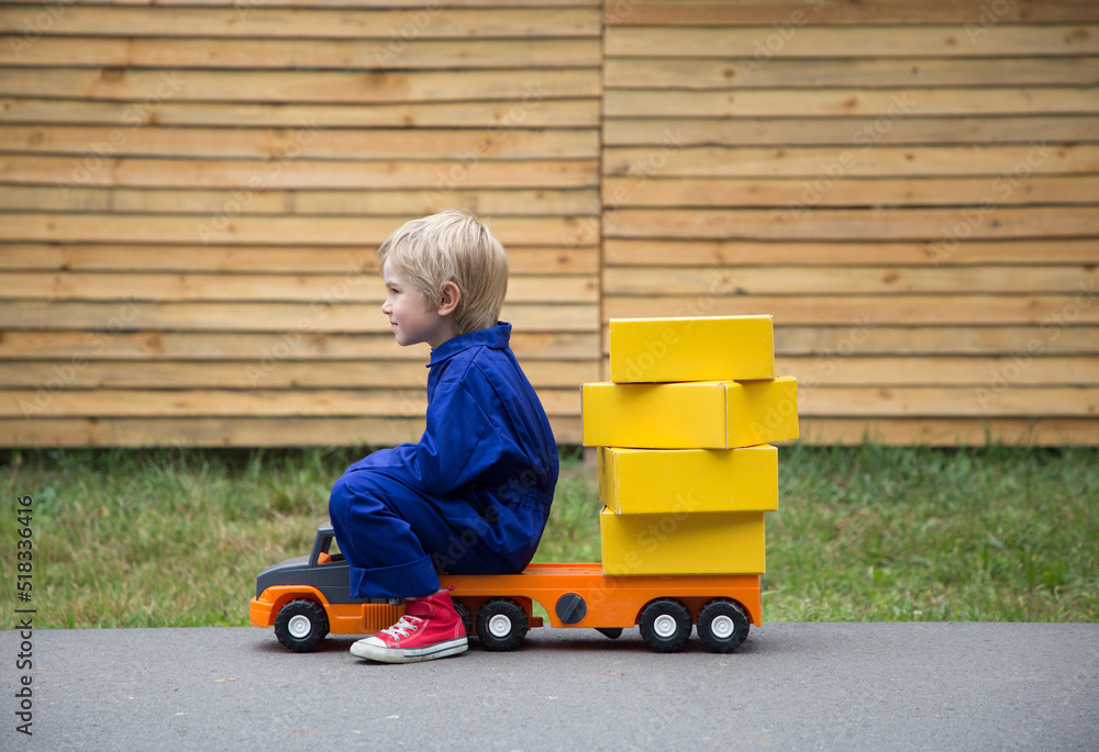 6-year-old boy in a blue overalls - uniform sits on a large toy car - a ...