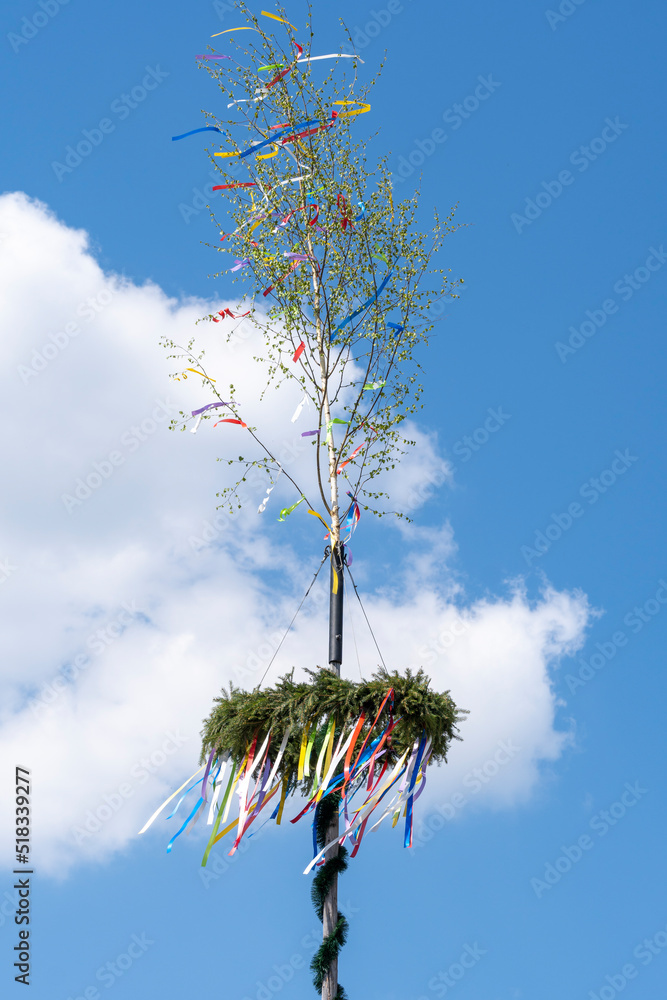 Maypole with wreath with ribbons in Germany against a sky with clouds ...