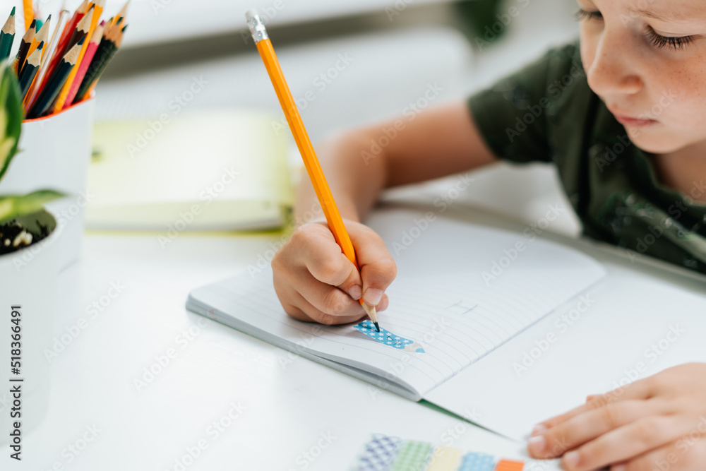 School kid boy studying at home with book, draw in notepad and doing ...