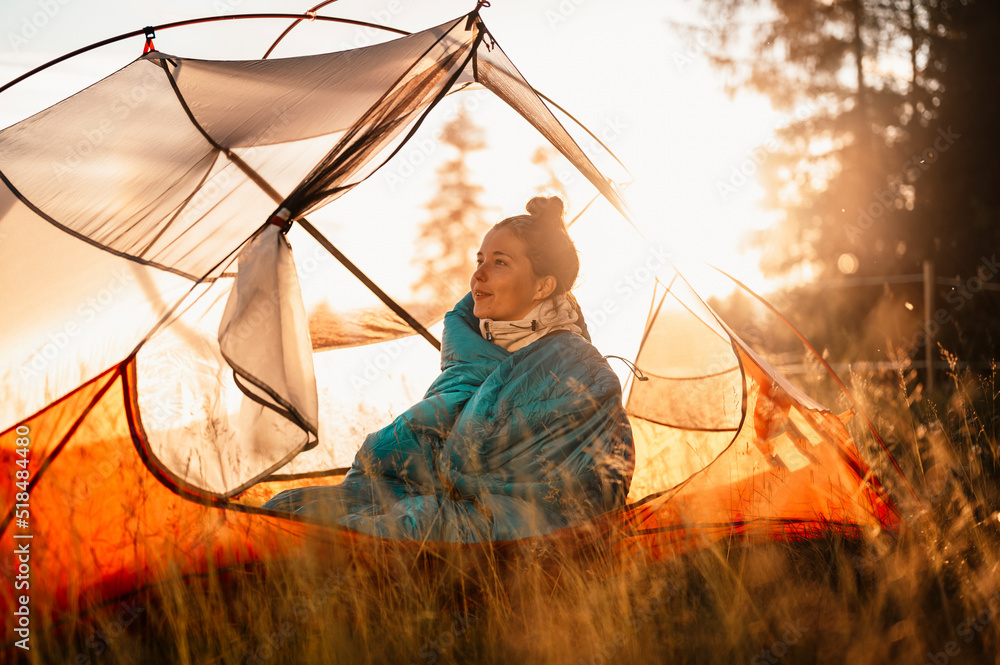 Woman relaxing and lie in a sleeping bag in the tent. Sunset camping in ...