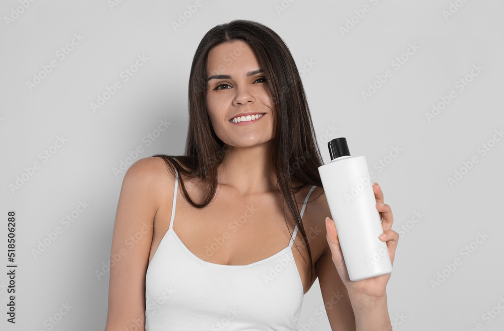 Beautiful young woman holding bottle of shampoo on white background ...
