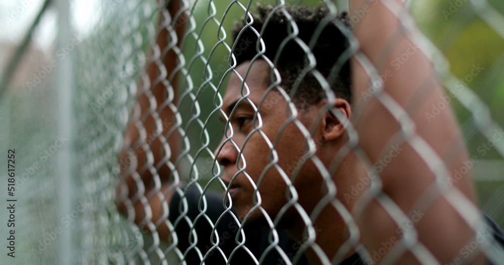 African mixed race man standing behind metal fence. Pensive black guy ...