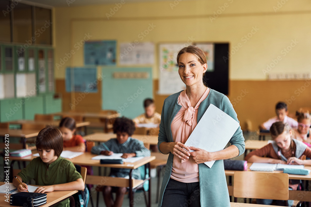 Foto de Happy elementary school teacher in classroom looking at camera ...