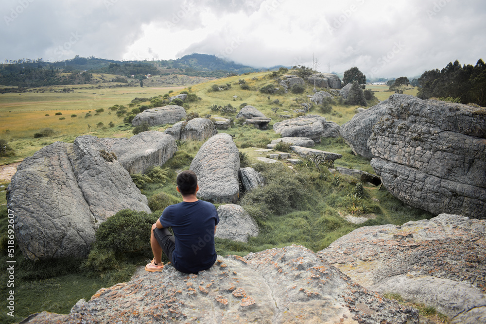 Joven sentado en una zona rocosa observando el paisaje de antiguas ...